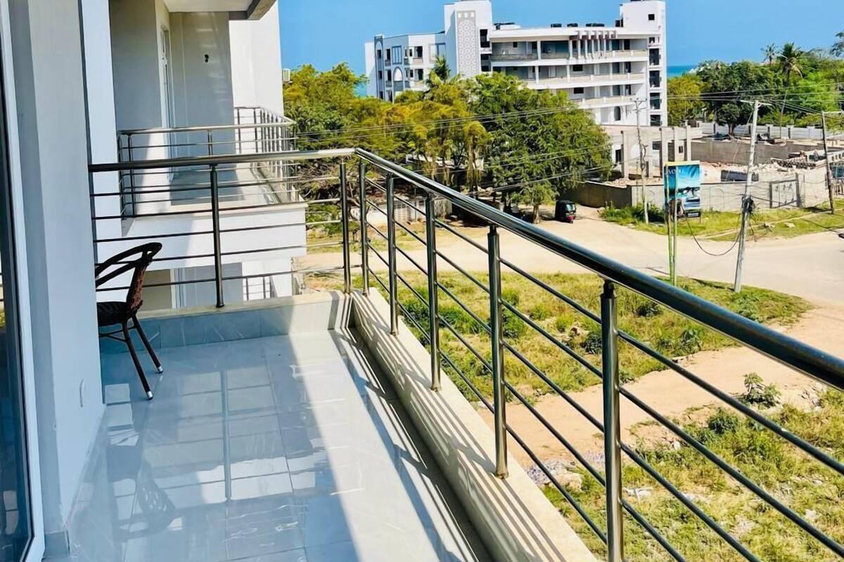 Uma varanda com uma cadeira, guarda-corpo e vista para edifícios e vegetação.