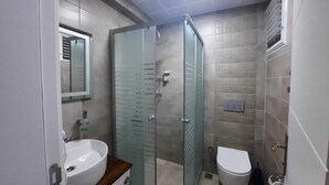 Casa de banho com cabine de chuveiro em vidro, pia branca e sanita.