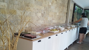 Disposição de buffet com estações de comida cobertas, uma planta em vaso e uma pessoa servindo.