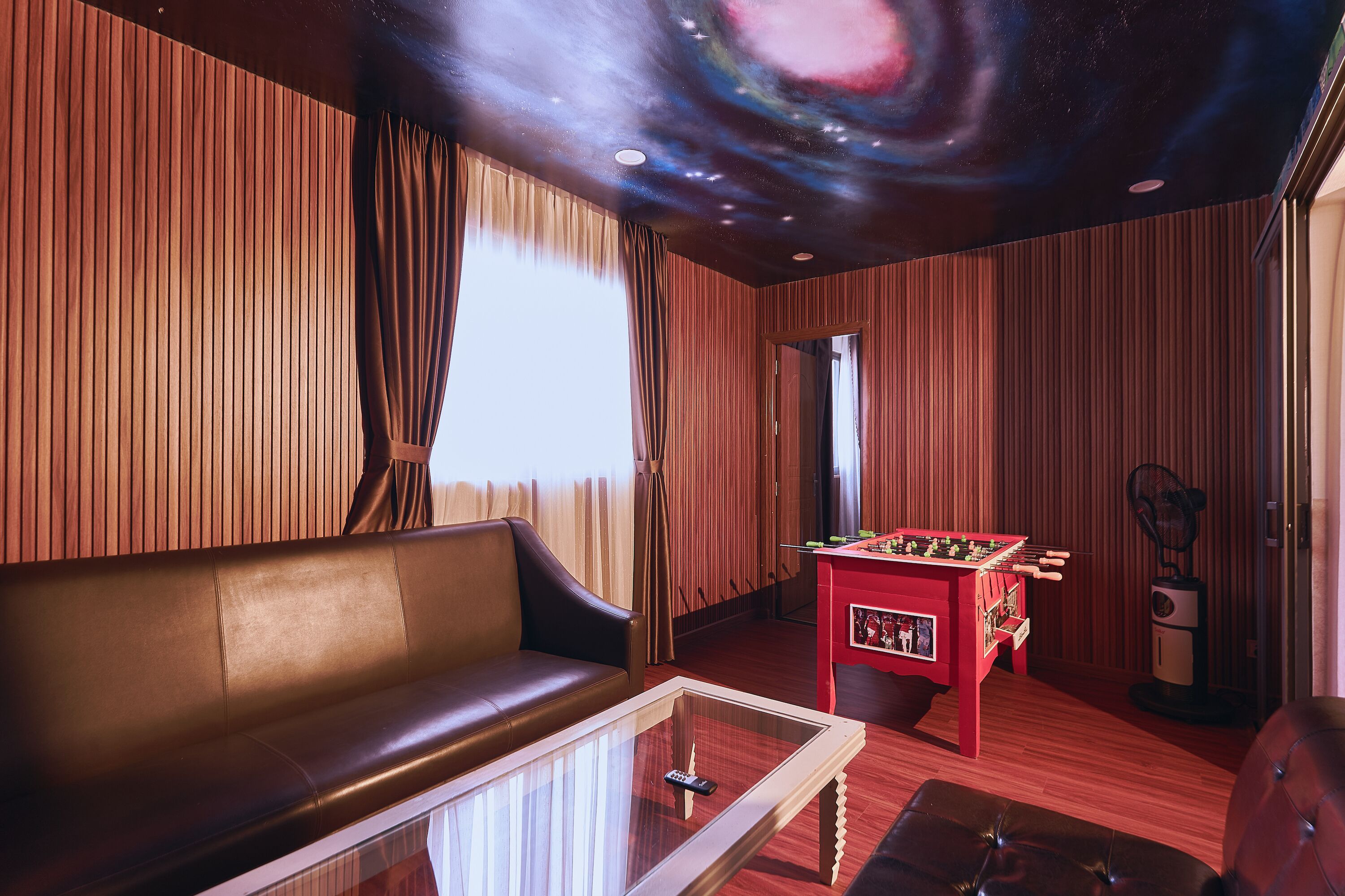Quarto com sofá, mesa de centro de vidro, mesa de pebolim e teto com mural de galáxia.