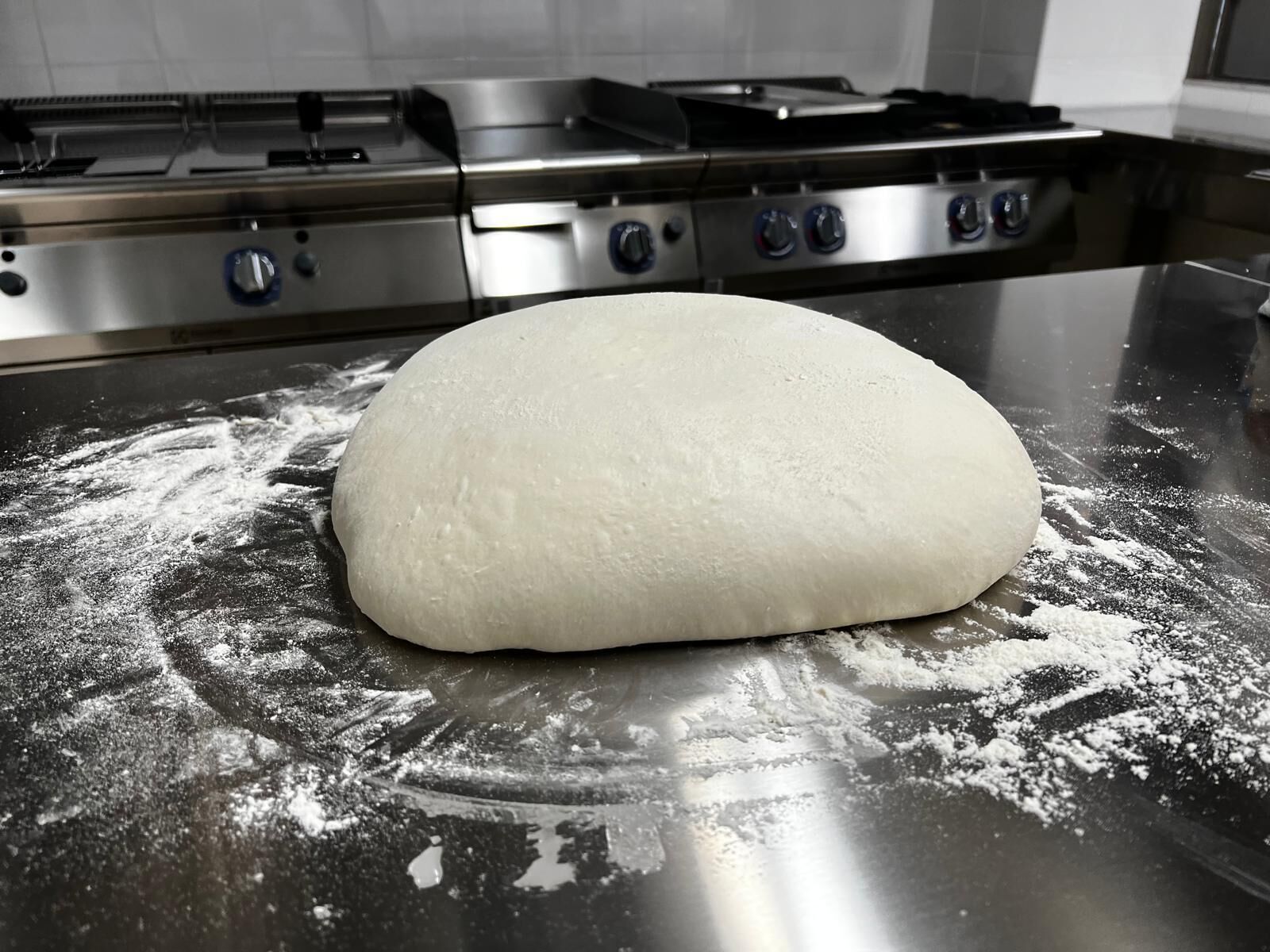 Uma cozinha com uma massa redonda grande e branca sobre uma superfície enfarinhada.