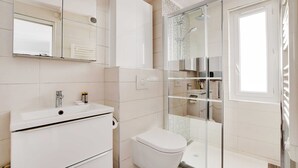 Um banheiro moderno com box de vidro, pia branca e vaso sanitário.