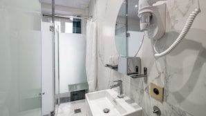 Casa de banho moderna com cabine de duche em vidro, lavatório branco e secador de cabelo fixo.