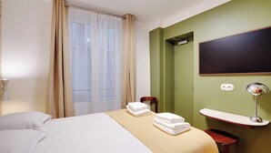 Quarto de hotel com cama, mesa de cabeceira, espelho e janela com cortinas.