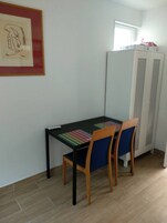 Uma pequena área de refeições com uma mesa, duas cadeiras, um armário branco e um quadro na parede.