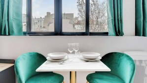 Uma área de refeições com uma mesa posta para dois, duas cadeiras e vista para edifícios pela janela.