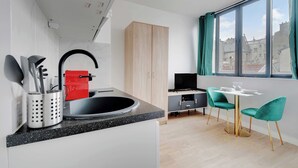 Cozinha moderna com bancada preta, eletrodoméstico vermelho e armário de madeira. Há uma área de refeições com mesa redonda e duas cadeiras verde-água.
