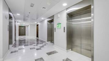Um corredor limpo e moderno com piso xadrez, dois elevadores e uma porta no final.