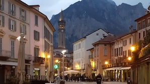 Uma praça com edifícios, um campanário e montanhas ao fundo.