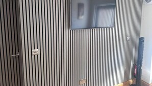Quarto com parede listrada, TV de tela plana fixada na parede, uma porta e extintor de incêndio.