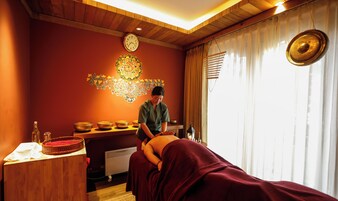 Sala de massagem com teto de madeira, relógio de parede, um detalhe decorativo, mesa de massagem e janela com cortinas.