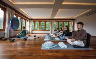 Aula de yoga em um espaço com piso de madeira, janelas amplas e vista para o verde.
