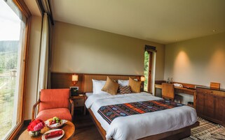 Quarto de hotel com cama, poltrona, mesa de cabeceira, escrivaninha e vista para o exterior.