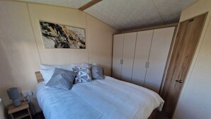 Quarto com cama, mesa de cabeceira, abajur e guarda-roupa.