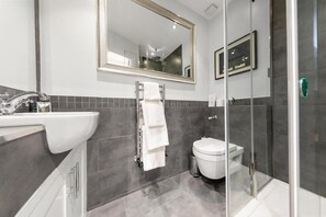 Uma casa de banho moderna com um espelho grande, lavatório, sanita e cabine de duche com vidro.