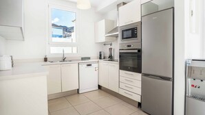 Cozinha moderna com armários brancos, eletrodomésticos de aço inoxidável e janela com vista para o exterior.