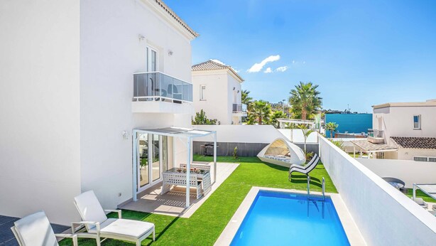 Uma área de piscina moderna com vista clara para o mar, zona de estar coberta e um jardim bem cuidado.