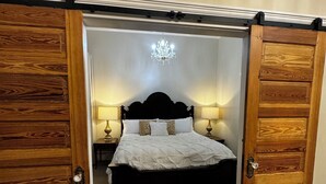 Quarto com cama, duas mesas de cabeceira com abajures, um candelabro e portas de madeira.