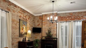 Um quarto com parede de tijolos, lareira, televisão, dois poltronas, uma mesa e um candelabro.