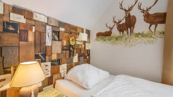 Quarto com cabeceira de madeira, cama com roupa de cama branca, mesa de cabeceira com abajur e um mural na parede com veados.