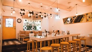 Uma área de bar com piso xadrez, um balcão longo e vários bancos.