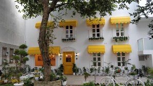 Um pátio com um edifício branco, toldos amarelos e plantas em vasos.