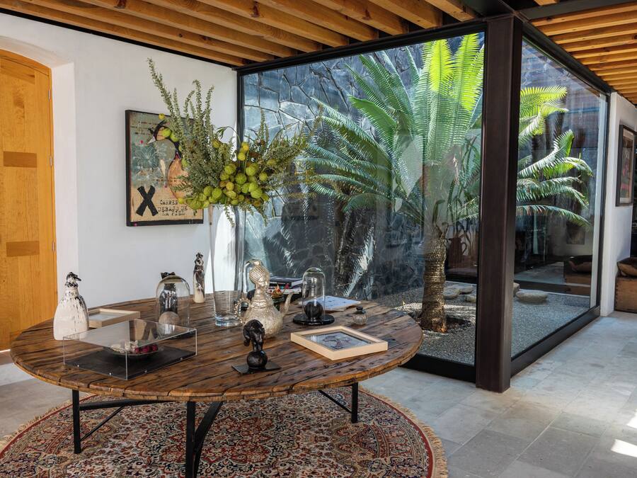 Um interior moderno com uma mesa de madeira, objetos decorativos e uma grande janela de vidro com vista para um jardim.