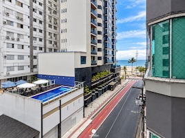 Um hotel com vários andares, piscina no terraço, ciclovia vermelha na rua e vista para a praia.