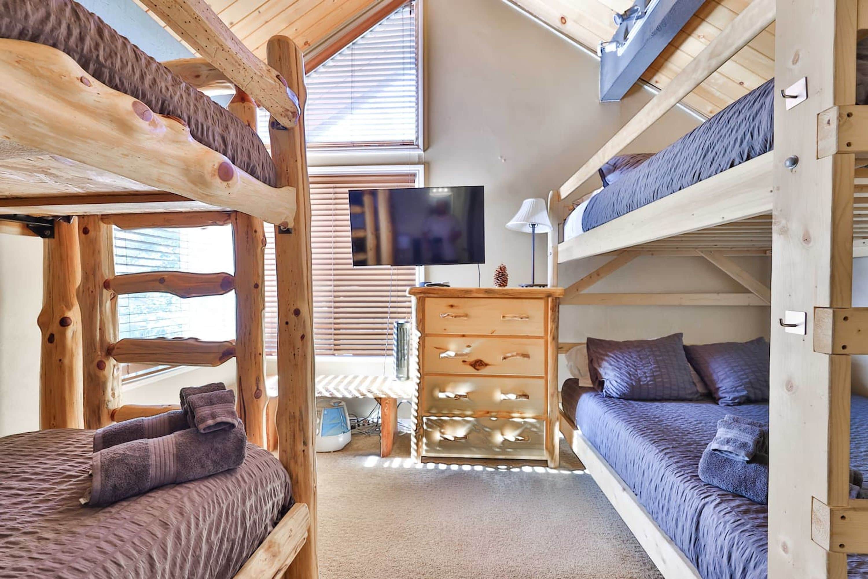 Interior de uma cabana de madeira com beliches, uma televisão e um aparador de madeira.