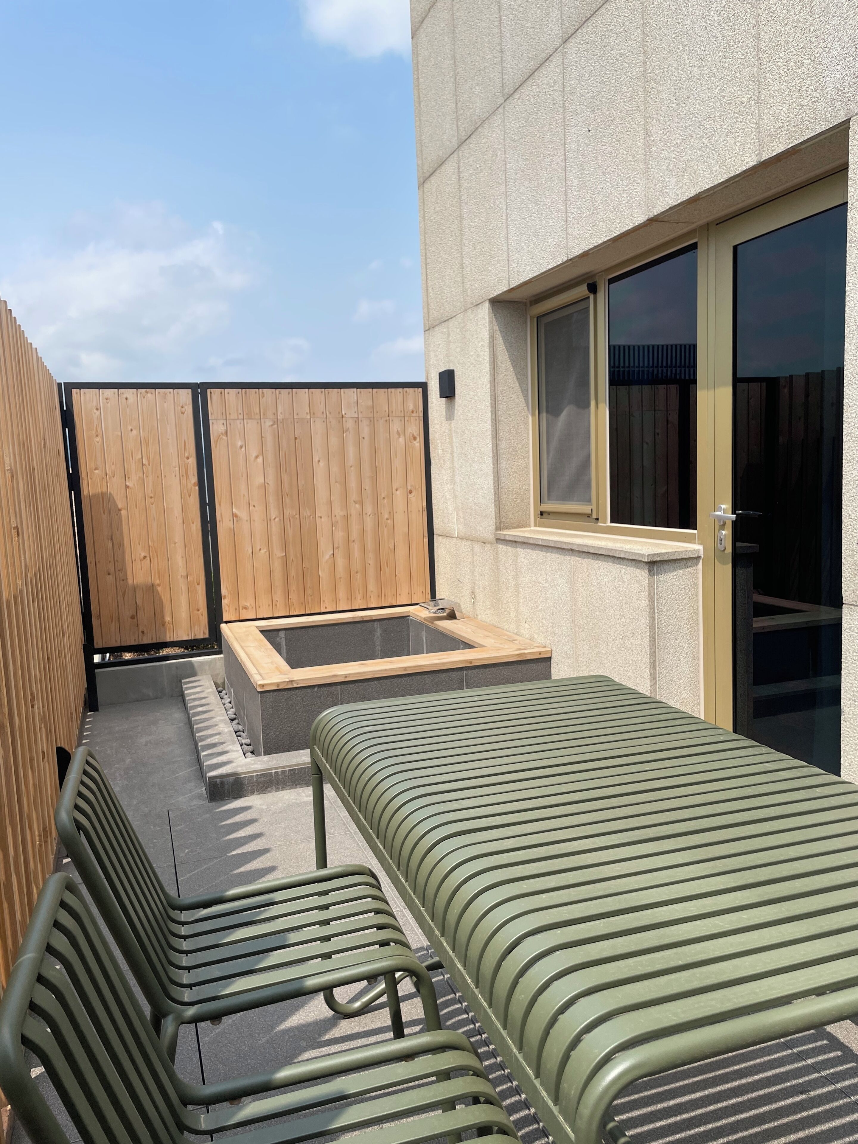 Terraço no telhado com cerca de madeira, banheira de hidromassagem e cadeiras de lounge de metal verde.