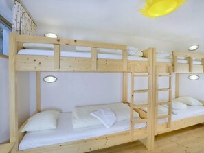 Uma cama beliche com escada, roupa de cama branca e luminária no teto.