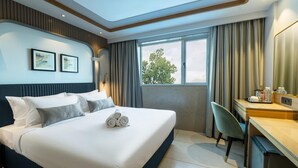 Quarto de hotel moderno com uma cama grande, uma escrivaninha e vista para árvores pela janela.