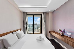 Quarto de hotel com uma cama grande, vista da cidade através de uma varanda e painel de madeira decorativo na parede.