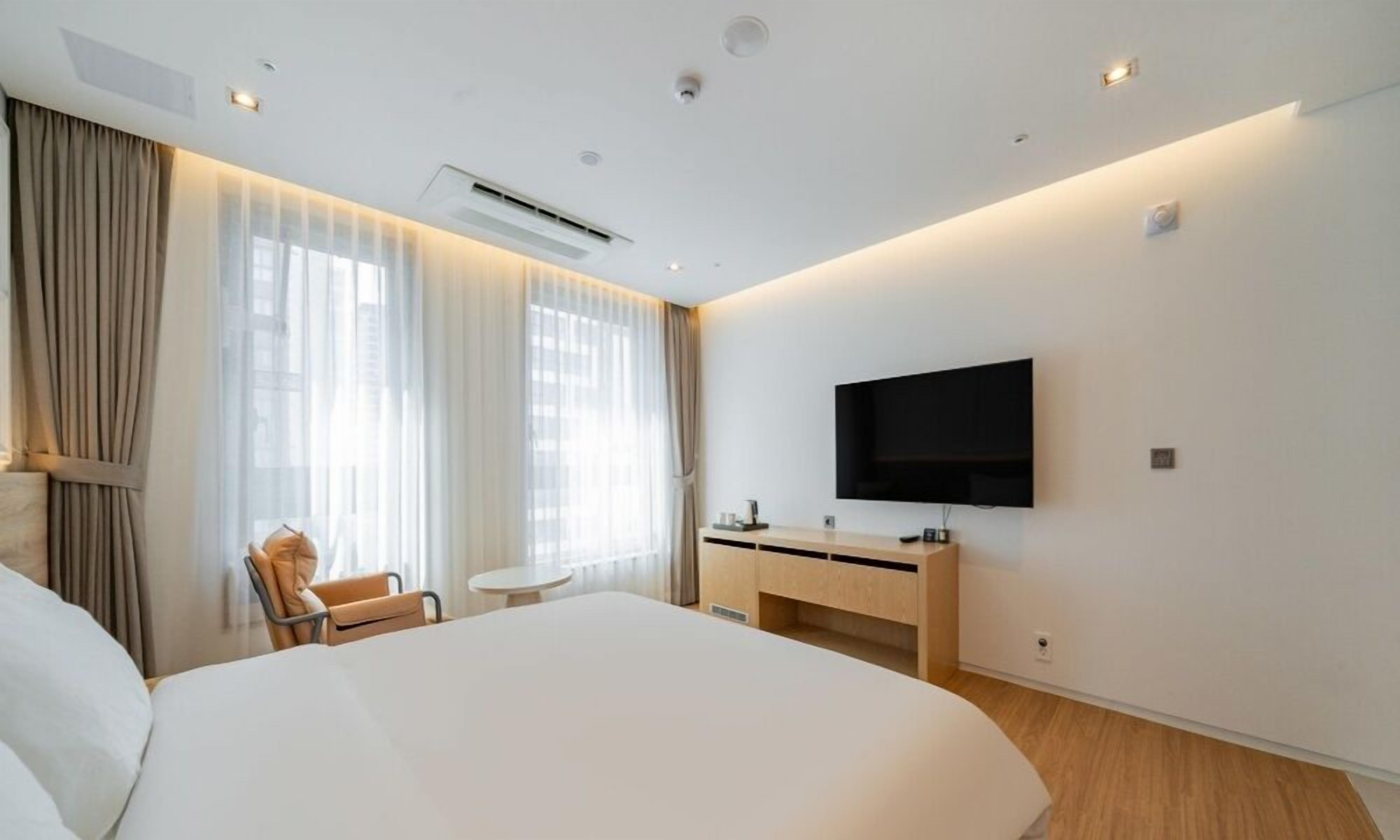 Quarto de hotel com uma cama grande, uma escrivaninha com televisão de tela plana, uma cadeira e uma mesa pequena.