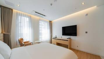 Quarto de hotel com uma cama grande, uma escrivaninha com televisão de tela plana, uma cadeira e uma mesa pequena.