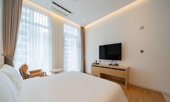 Quarto de hotel com uma cama grande, uma televisão, uma mesinha e uma cadeira.