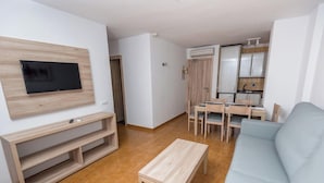 Uma sala de estar moderna com uma TV de tela plana presa a um painel de madeira, um sofá azul claro, uma mesa de centro de madeira e uma área de jantar com uma mesa e cadeiras de madeira.