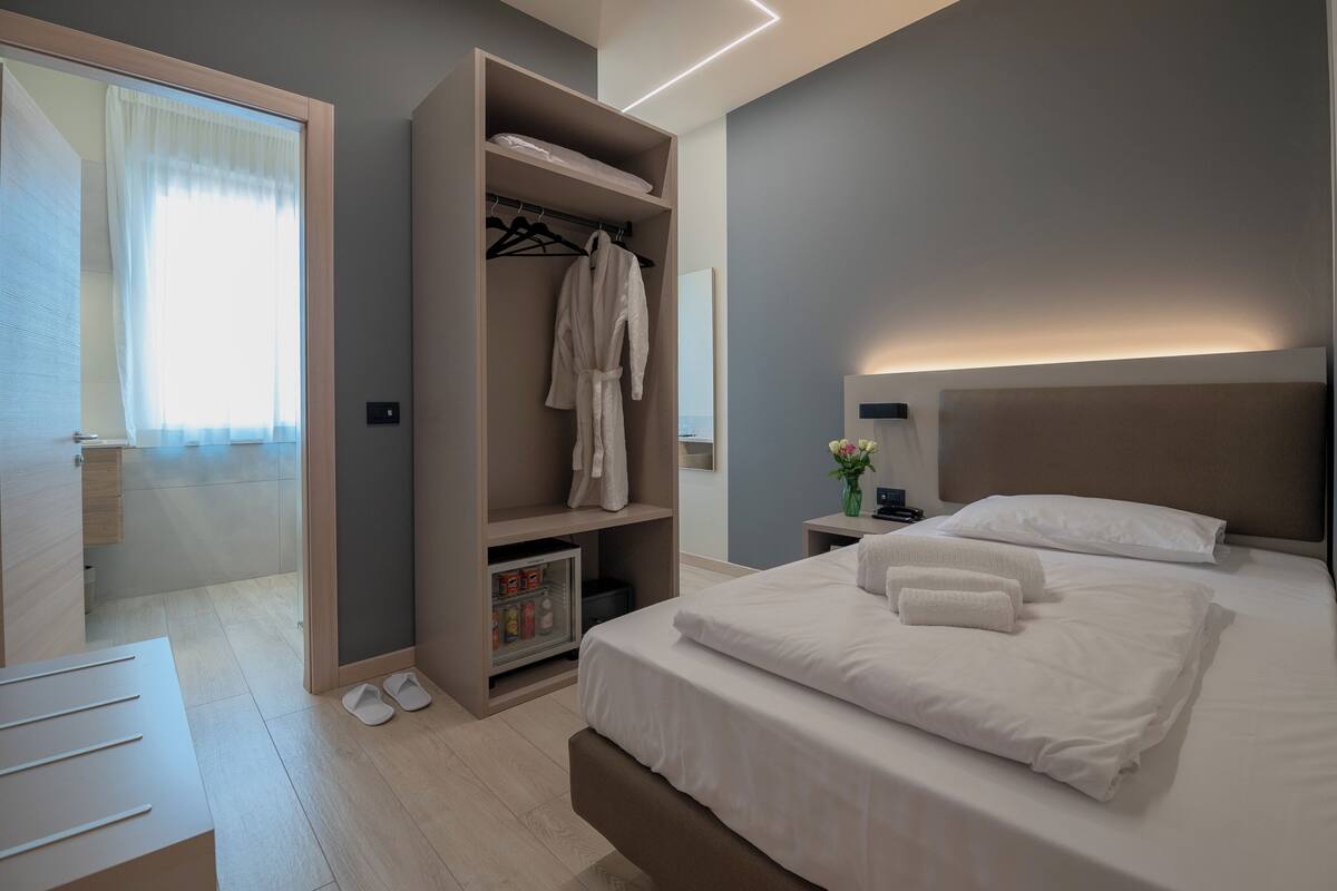 Quarto de hotel moderno com uma cama grande, um closet espaçoso e um banheiro com chuveiro de vidro.