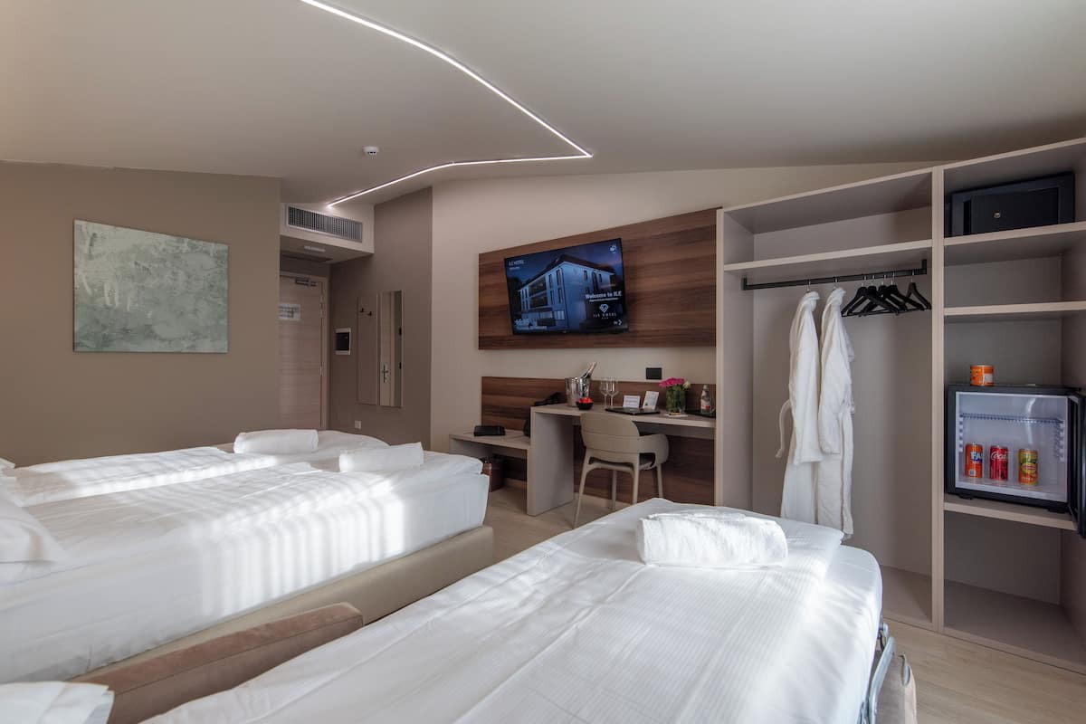 Quarto de hotel com duas camas, uma escrivaninha, televisão, guarda-roupa e mini-frigorífico.