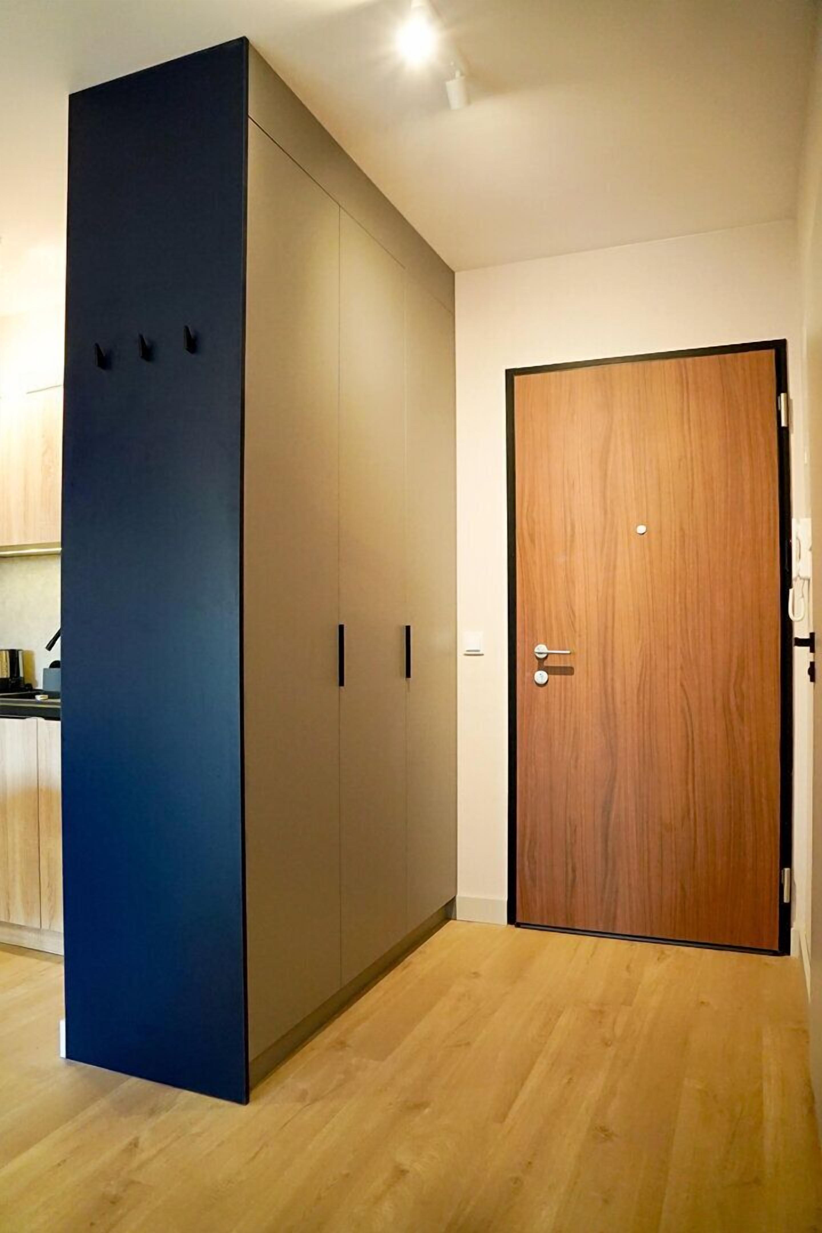 Quarto com um guarda-roupa grande, porta de madeira e área de cozinha ao fundo.