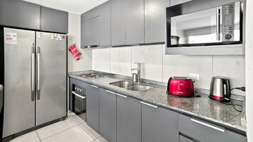Cozinha com armários cinza, geladeira de aço inoxidável, cafeteira vermelha e chaleira.