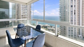 Varanda com mesa e cadeiras de vidro, com vista para a cidade e o mar.