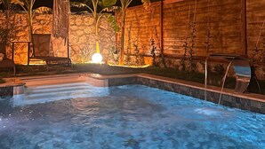 Piscina com parede de pedra e cerca de madeira ao fundo.