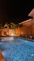 Piscina com parede de pedra e cerca de madeira ao fundo.