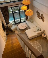 Sala de estar moderna com um sofá grande, uma mesa de centro e uma escadaria que leva a uma área externa com piscina.