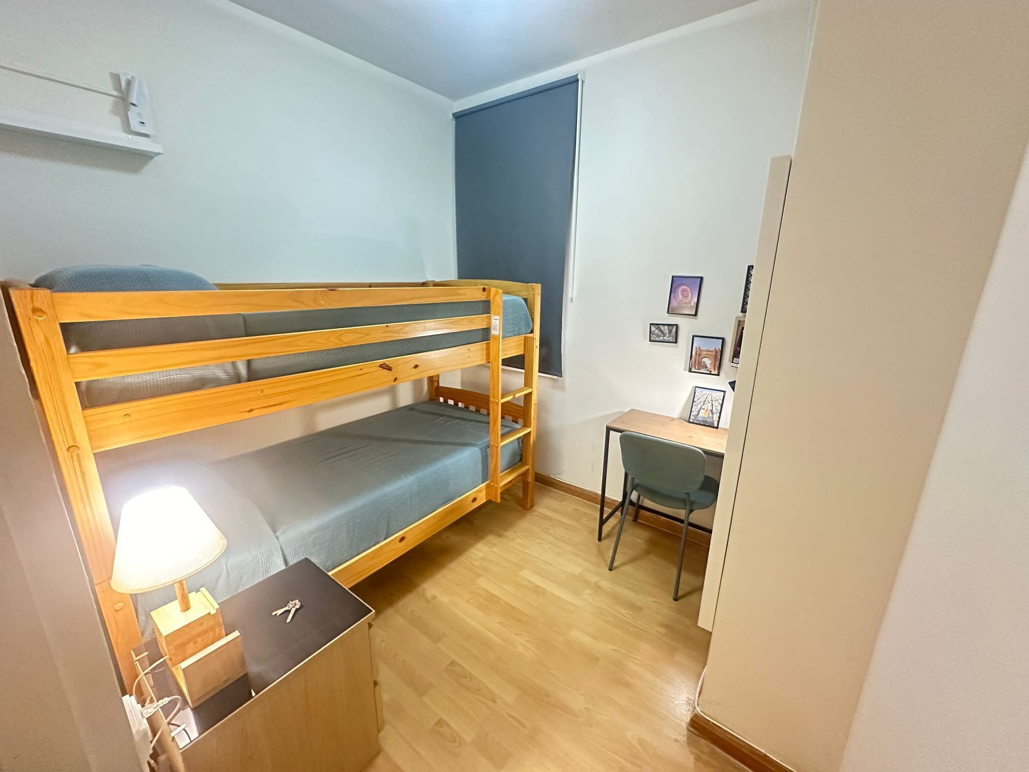 Quarto compacto com beliche, escrivaninha, cadeira, luminária e um pequeno armário.