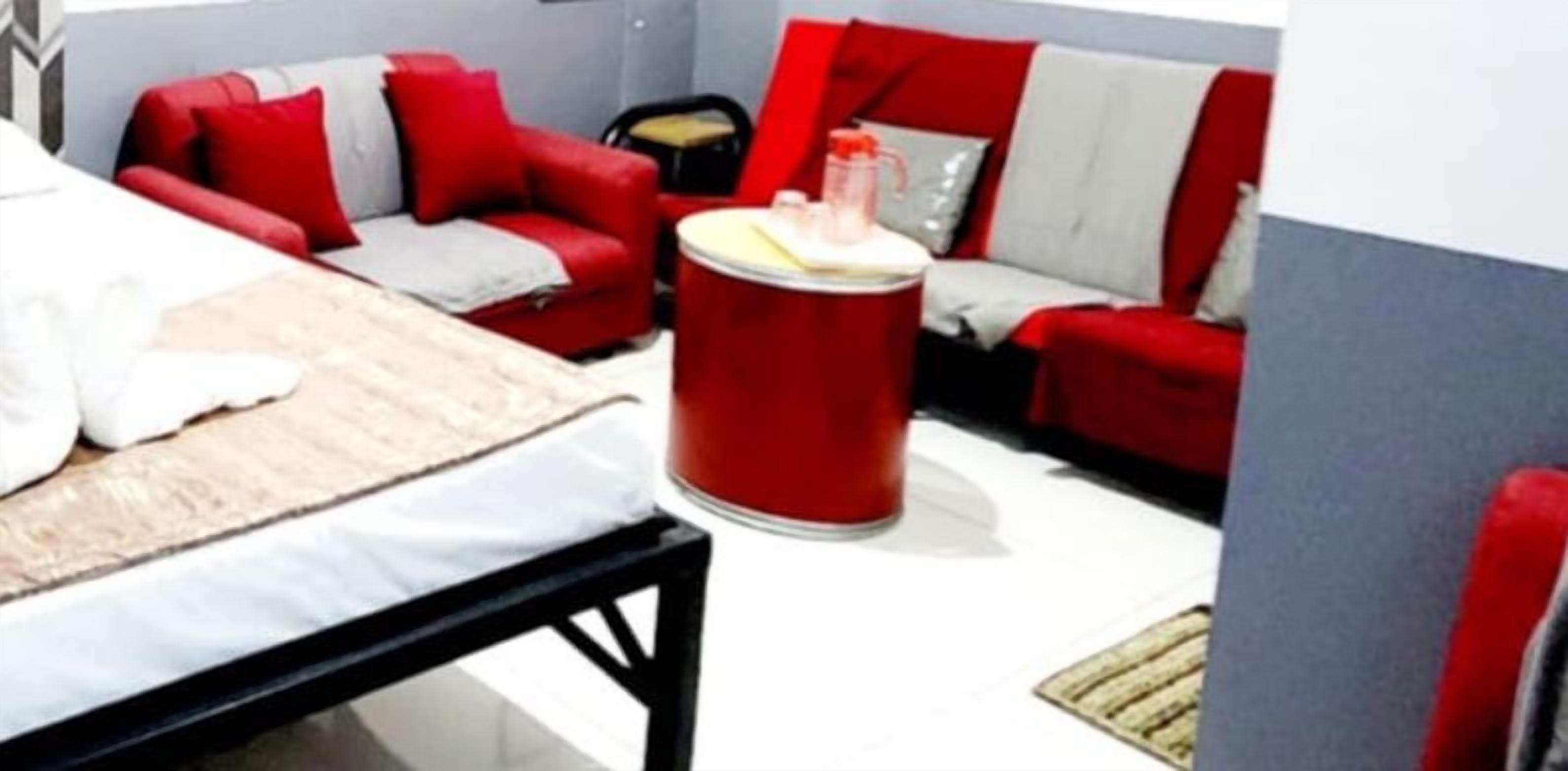 Um quarto com uma cama, um sofá vermelho e uma mesa vermelha com uma bebida.