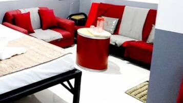 Um quarto com uma cama, um sofá vermelho e uma mesa vermelha com uma bebida.