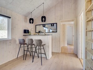Cozinha moderna com interior em madeira, área de bar com três banquetes e um espelho grande acima do balcão.