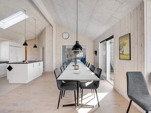 Uma cozinha moderna com uma ilha central, uma área de jantar com uma mesa comprida e cadeiras, e um relógio na parede.